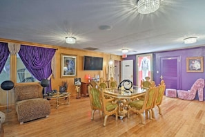 Uma sala de estar espaçosa com uma mesa redonda de madeira, cadeiras combinando, um sofá estampado com padrão de leopardo e uma televisão na parede.