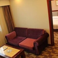Quarto de hotel com sofá vermelho, mesa lateral de madeira e tapete estampado.