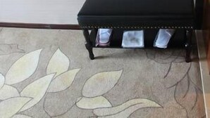 Um pequeno banco preto com detalhe decorativo, colocado sobre um tapete com motivos de lótus.