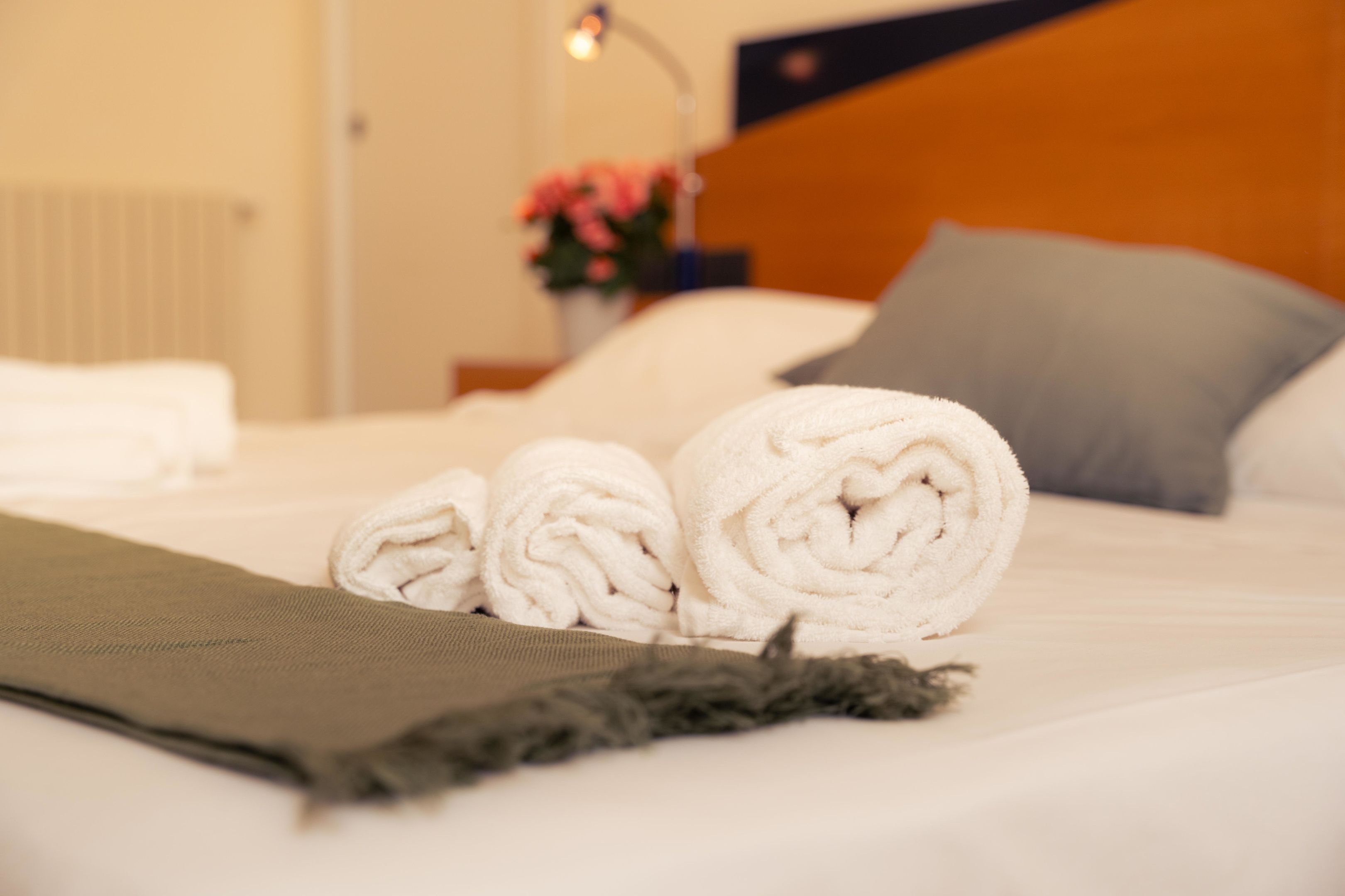 Cama bem arrumada com toalhas dobradas, um travesseiro cinza e um cobertor verde.