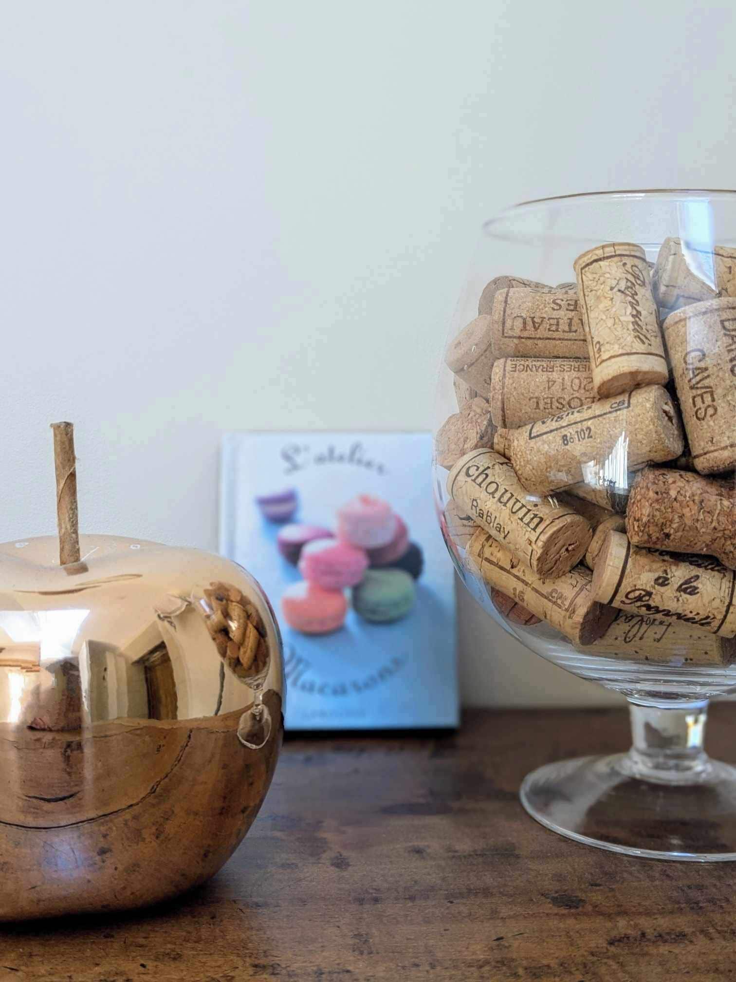 Uma taça decorativa cheia de rolhas de vinho e uma tigela metálica com alça.