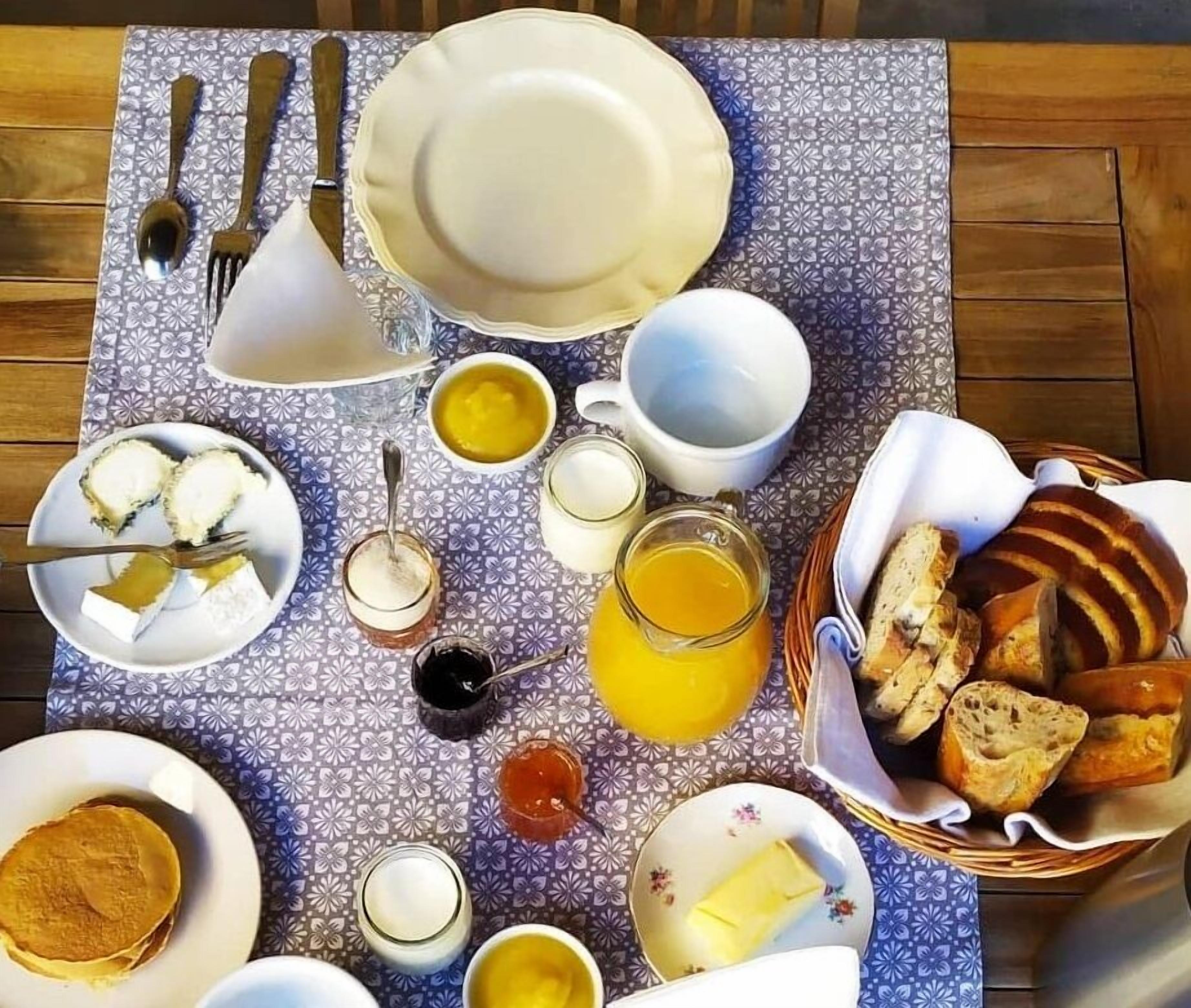 Uma mesa de café da manhã com pratos, talheres, uma cesta de pão e diversos acompanhamentos.