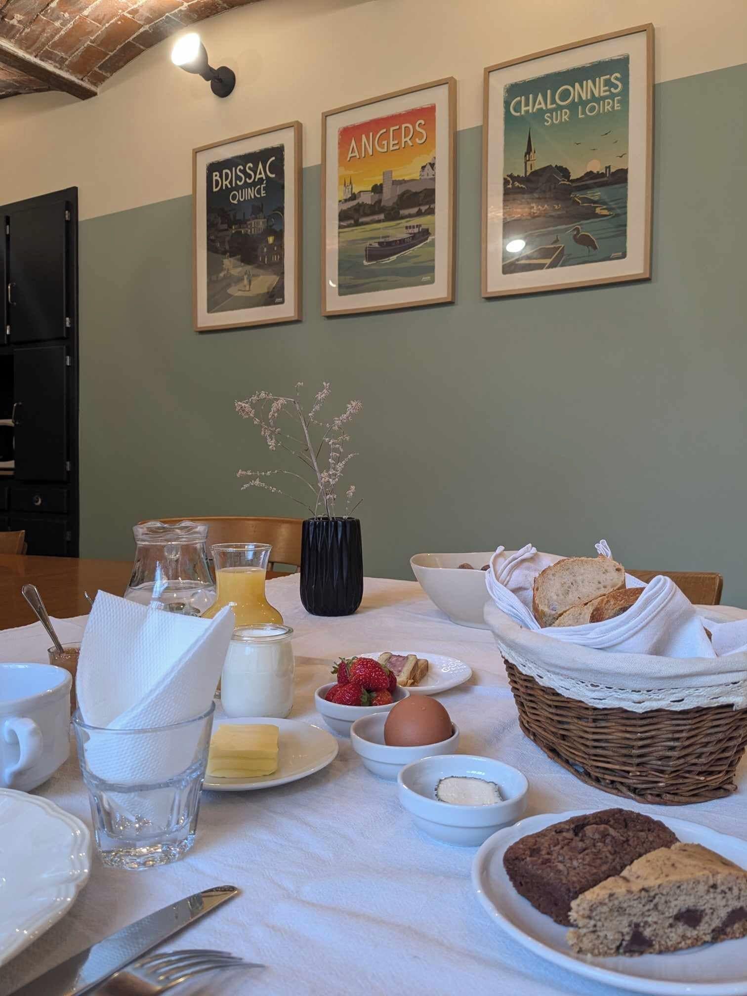 Uma mesa de café da manhã com diversos alimentos, uma cesta de pão e três quadros na parede.