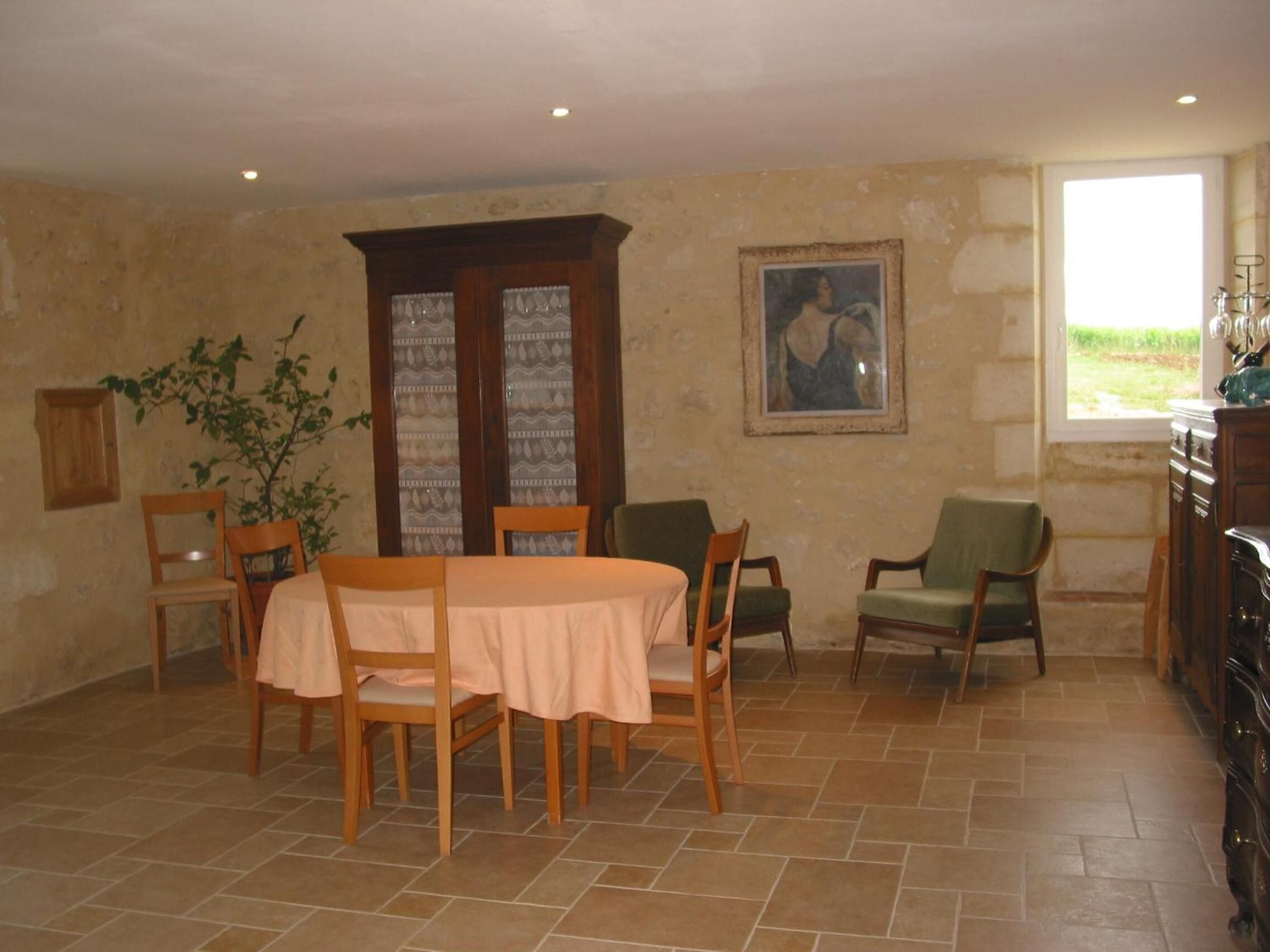 Uma sala de jantar com uma mesa posta para quatro pessoas, rodeada por cadeiras, um armário de madeira e uma janela com vista.