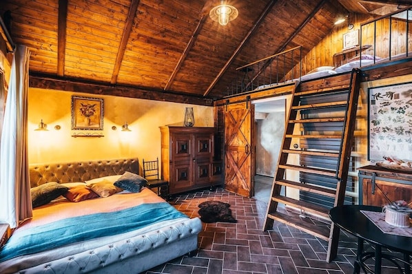Quarto rústico com cama, guarda-roupa de madeira, escada e parede com padrão floral.