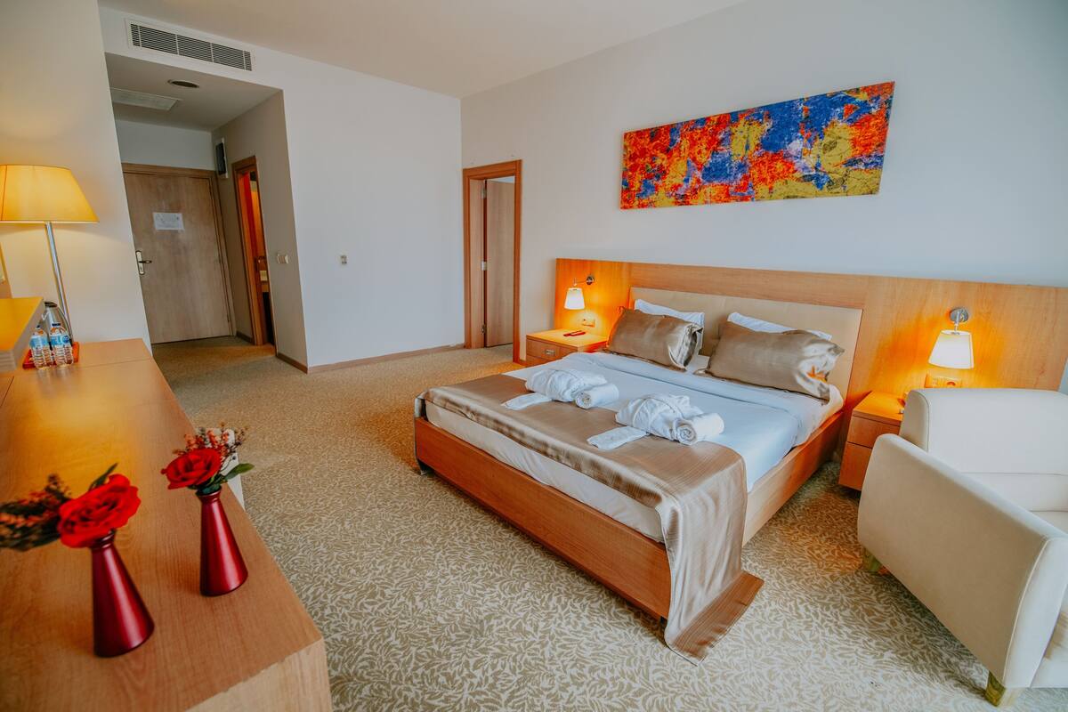 Quarto de hotel com cama, mesas de cabeceira, escrivaninha e uma cadeira.