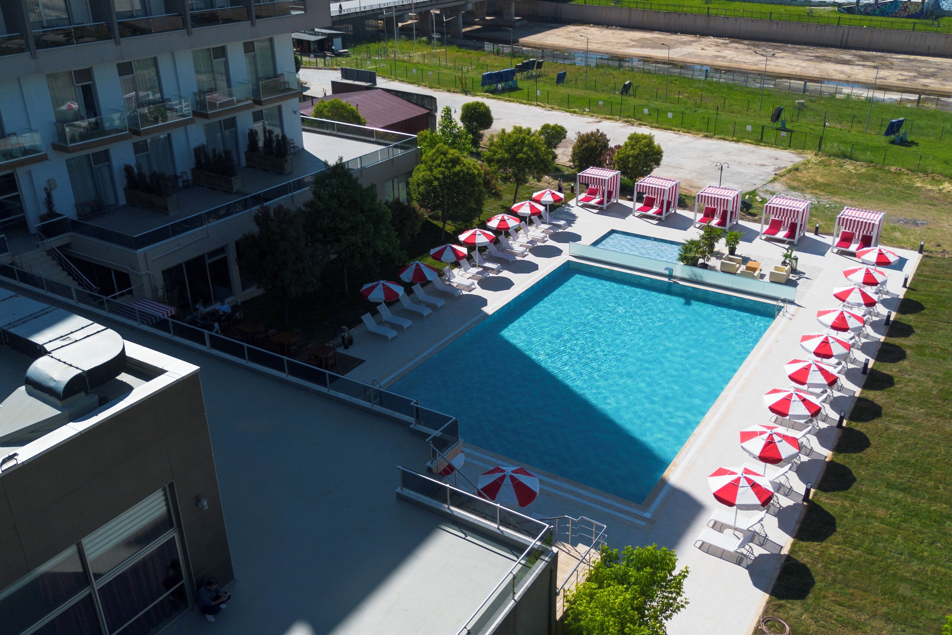 Uma piscina no terraço com espreguiçadeiras e guarda-sóis, cercada por um edifício com varandas e um espaço com gramado.