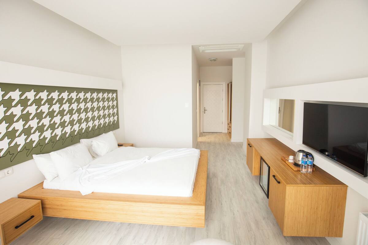 Quarto de hotel moderno com cama, mesa de cabeceira, televisão e um console de madeira.