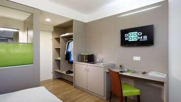 Quarto de hotel moderno com cama, escrivaninha com cadeira, cozinha compacta, televisão e closet espaçoso.