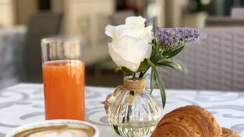 Uma mesa com um croissant, um copo de suco de laranja, uma xícara de café e um vaso decorativo com flores.