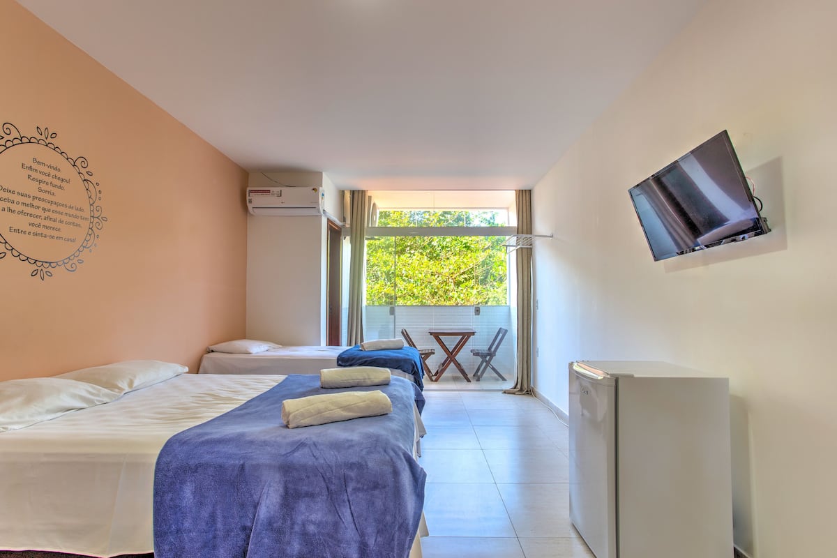 Quarto de hotel com duas camas, televisão e varanda com mesa e cadeiras.