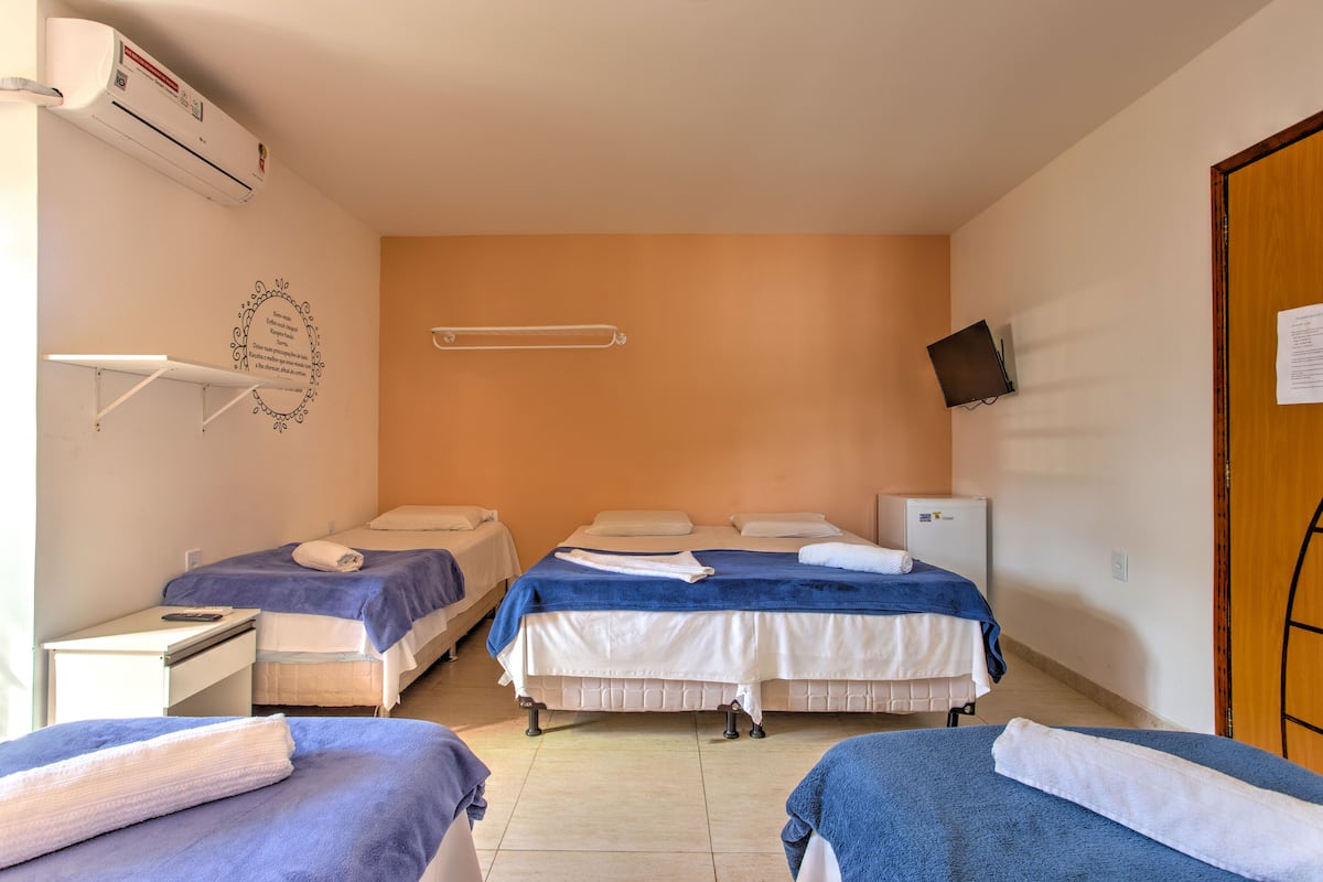 Quarto de hotel com duas camas de solteiro, uma escrivaninha, uma cadeira, uma TV e um ar condicionado.