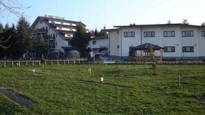Um campo gramado com um pavilhão e um edifício com várias janelas e um telhado plano.