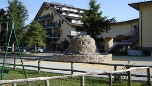 Um edifício com uma fonte de pedra, parquinho infantil e área de estacionamento.