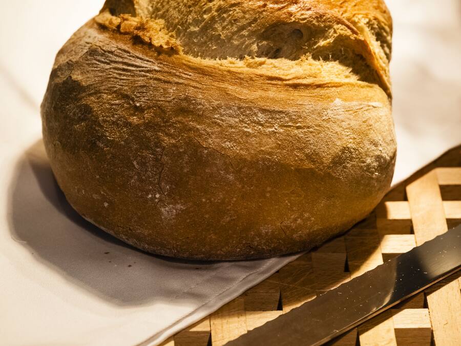Uma barra de pão sobre uma tábua de corte trançada, com uma faca ao lado.