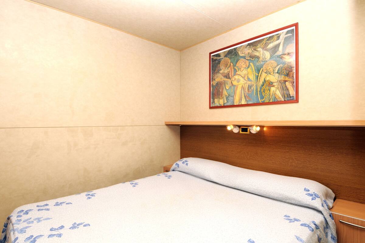 Um quarto com cama, cabeceira de madeira, um quadro na parede e mesa de cabeceira com luminária.