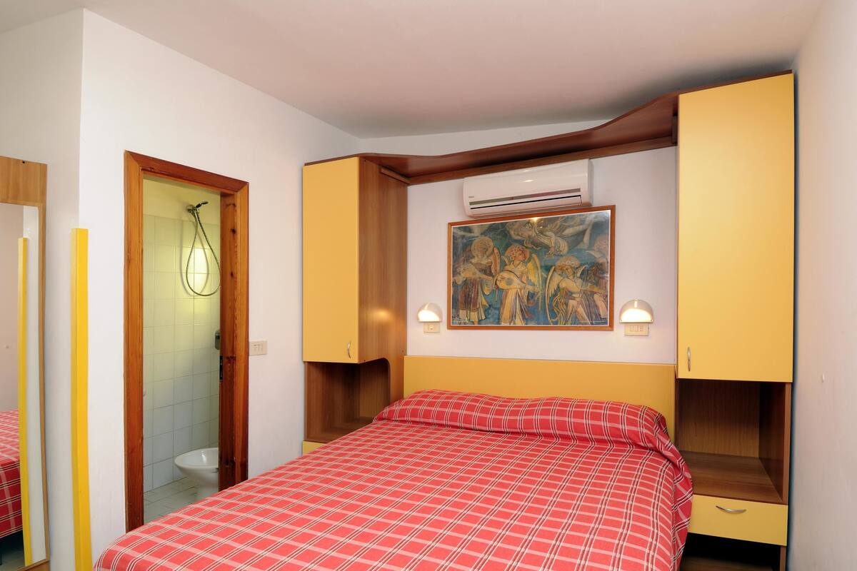 Quarto com cama, um quadro, ar condicionado e banheiro com chuveiro.