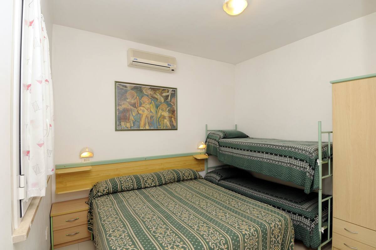 Quarto com beliches, cabeceira de madeira, ar condicionado fixado na parede, quadro emoldurado e abajur.