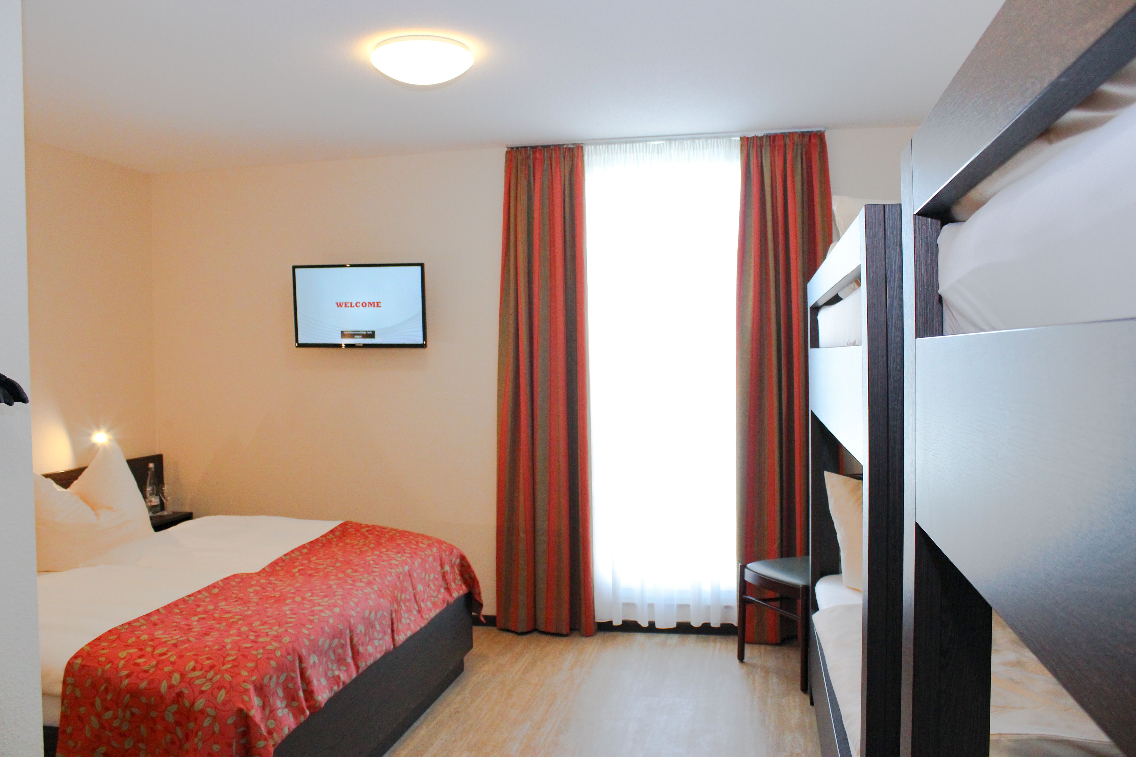 Quarto de hotel com cama, televisão, escrivaninha e janela com cortinas.