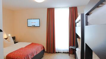 Quarto de hotel com cama, televisão, escrivaninha e janela com cortinas.