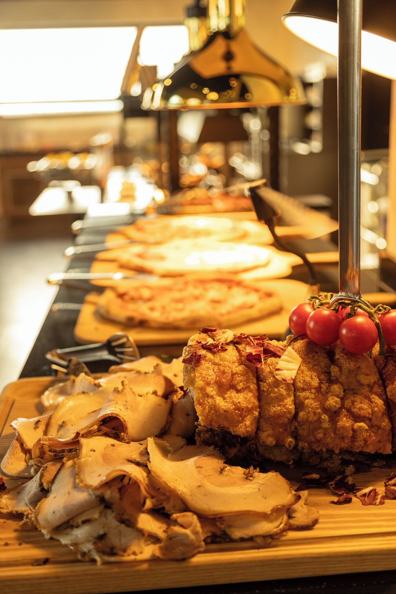 Buffet com diversos alimentos, incluindo carnes fatiadas e uma exposição de tomates em um galho.