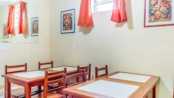Uma sala de jantar com mesas e cadeiras de madeira, obras de arte florais emolduradas nas paredes e uma janela com cortinas.