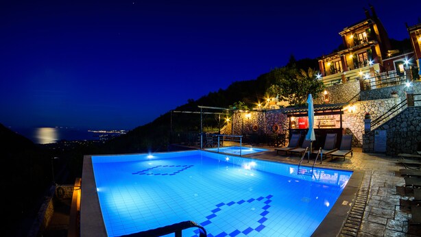 Piscina com deck revestido em azulejo, parede de pedra e área de bar com mesas ao ar livre.