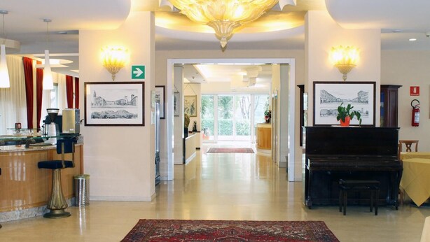 Um saguão de hotel com um lustre imponente, uma recepção, um piano e obras de arte emolduradas nas paredes.