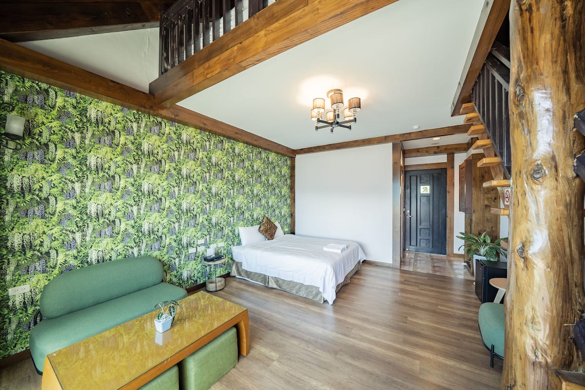 Um quarto com uma cama, um sofá verde, uma mesa de centro de madeira e uma parede com um padrão de folhas.