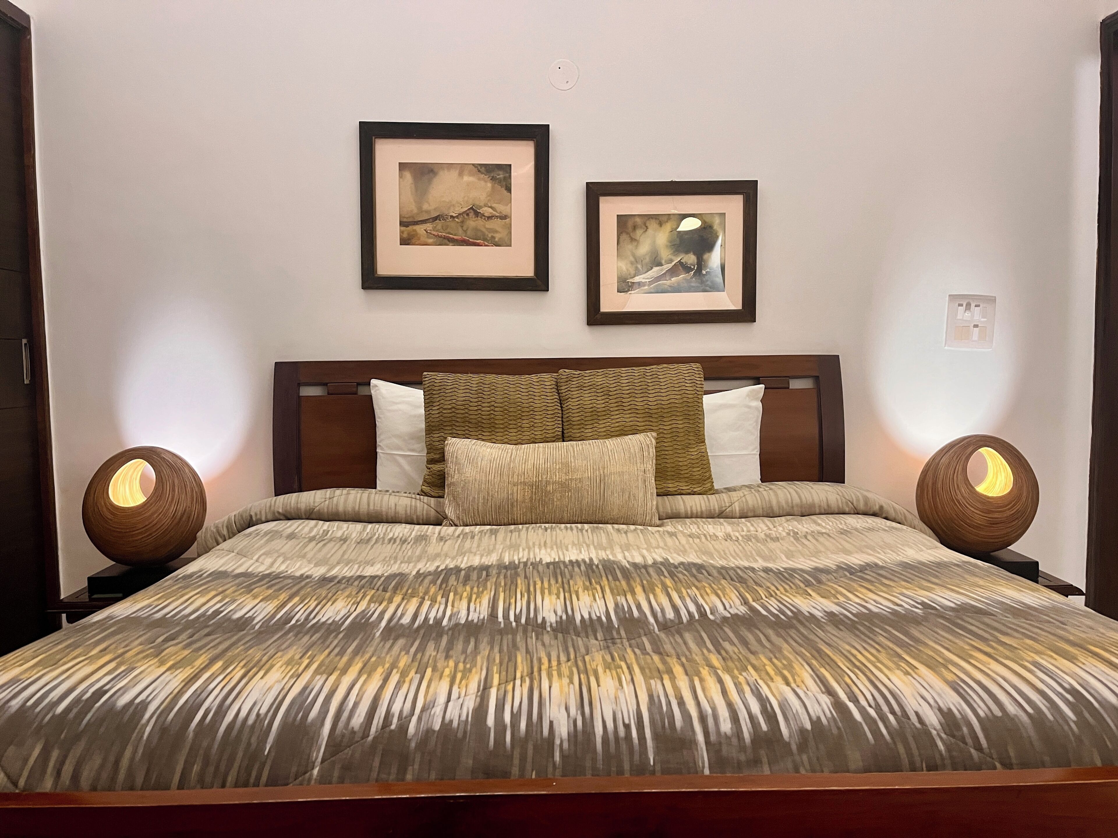 Uma cama com colcha estampada, duas imagens emolduradas na parede e duas luminárias fixadas na parede.