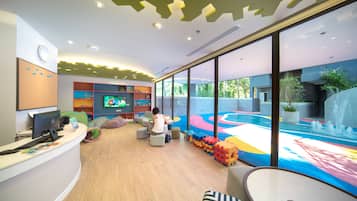 Uma área de recreação coberta moderna, com piscina, estruturas de jogos coloridas e uma tela de televisão.