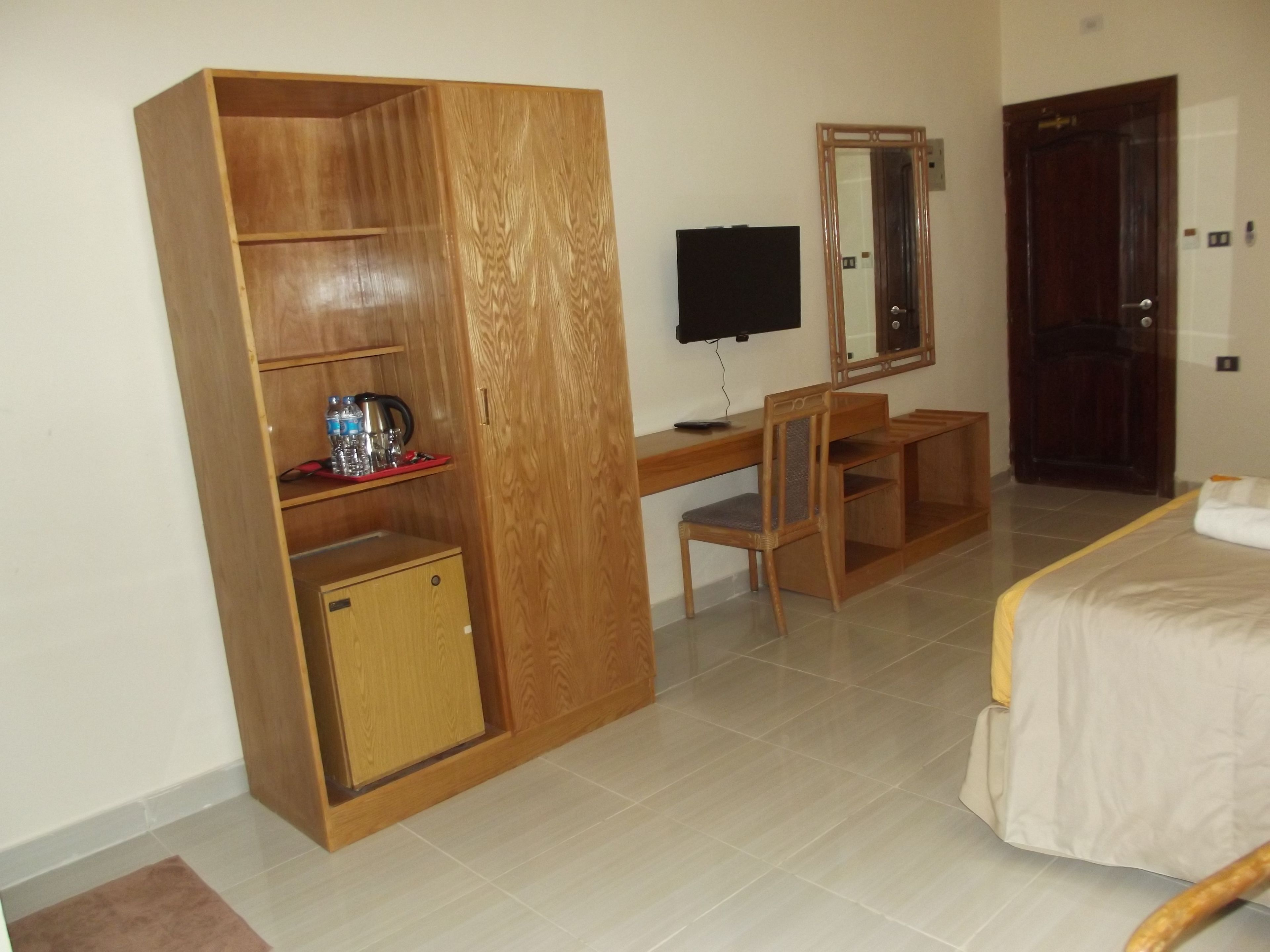 Quarto com cama, guarda-roupa de madeira, escrivaninha com cadeira, televisão e espelho.