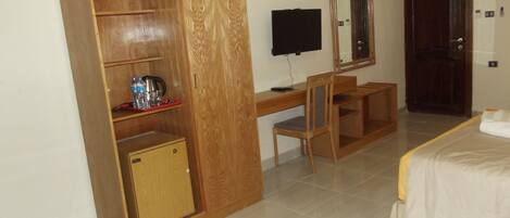 Quarto com cama, guarda-roupa de madeira, escrivaninha com cadeira, televisão e espelho.