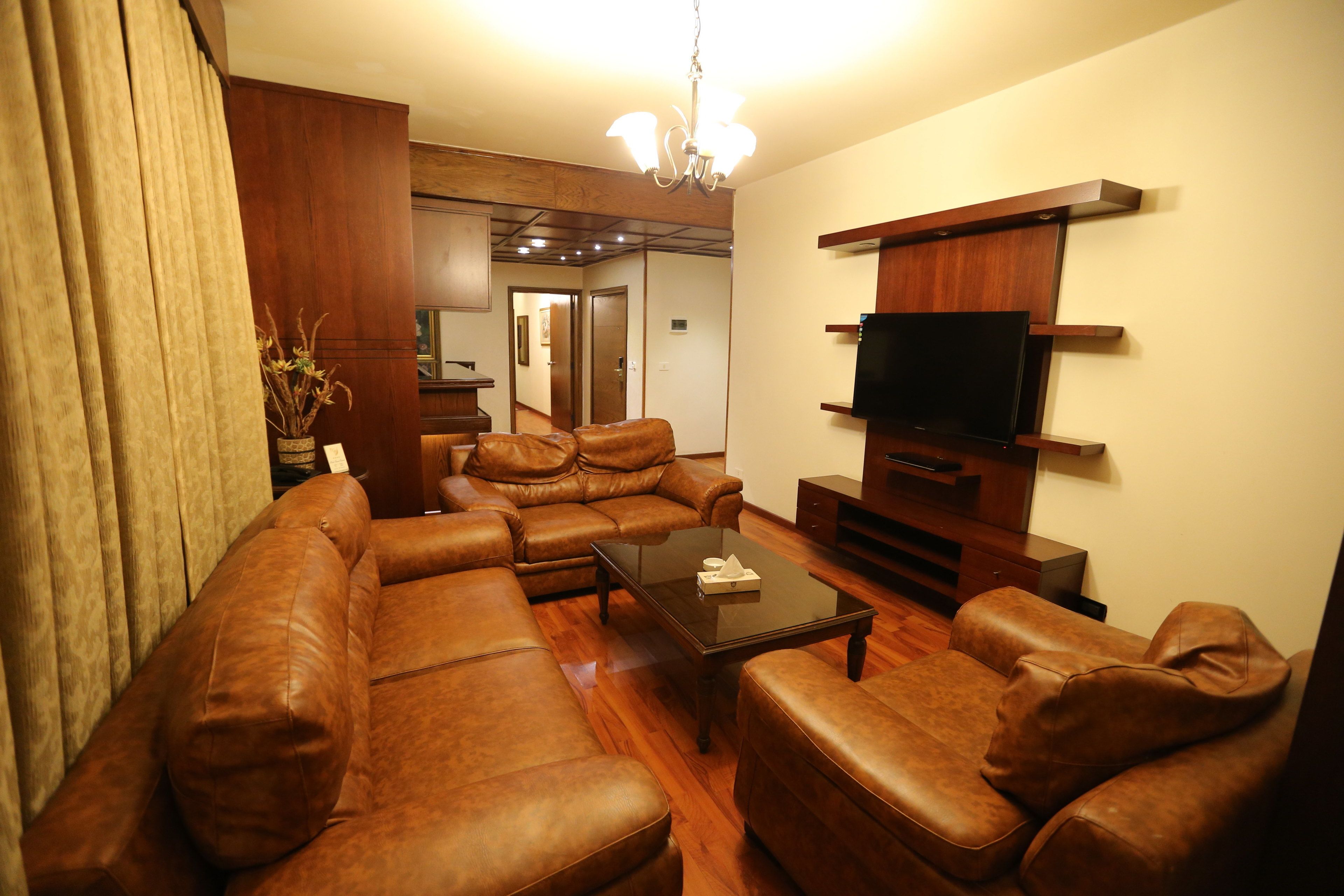 Uma sala de estar com sofá de couro marrom, mesa de centro de vidro e televisão de tela plana na parede.