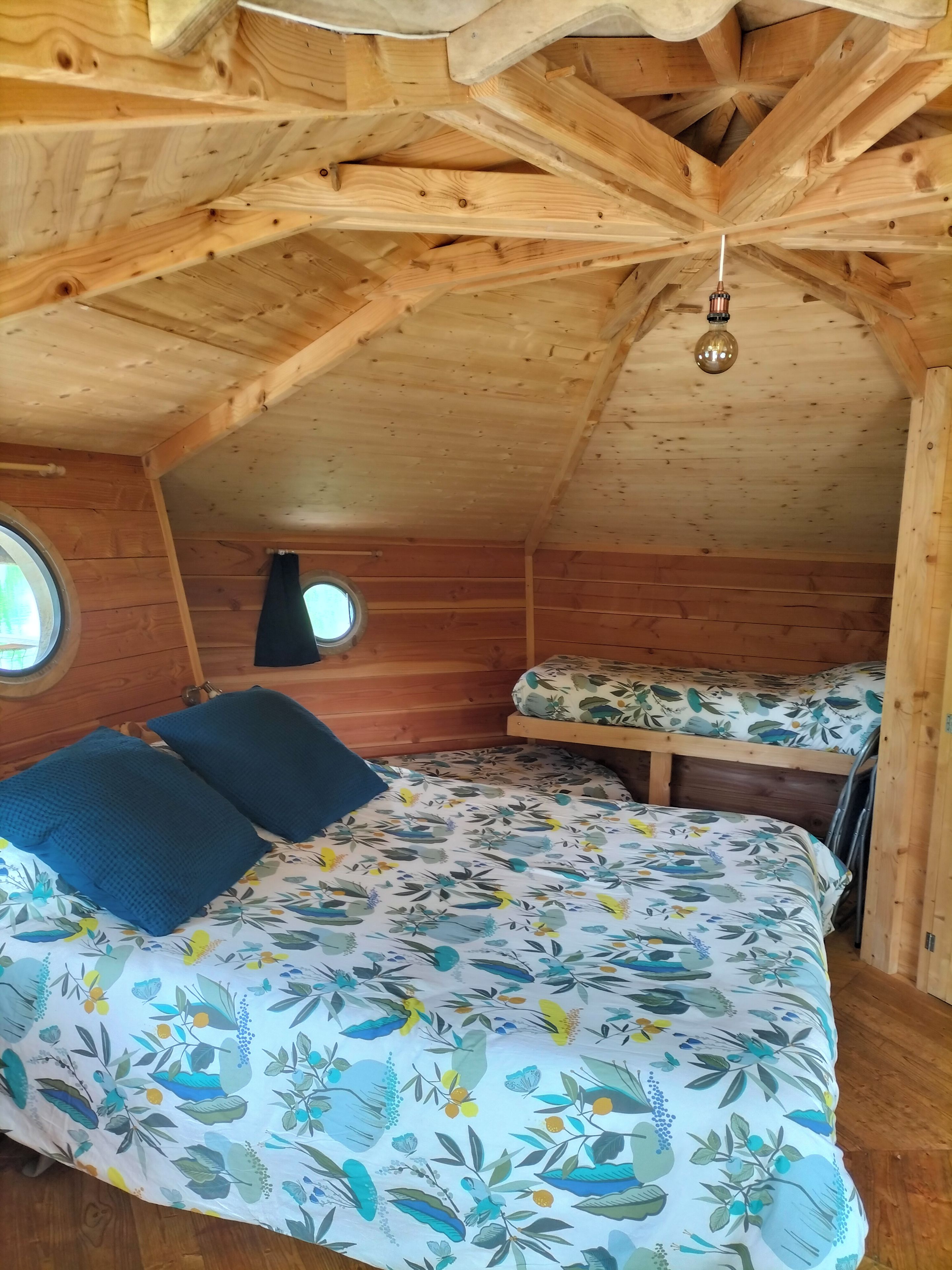 Um quarto de sótão acolhedor, com teto de madeira, beliche, janela redonda e luminária suspensa.