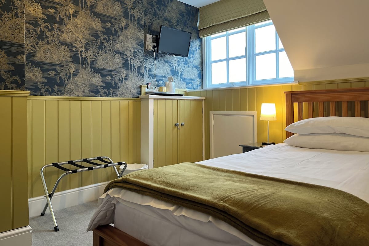 Quarto de hotel com uma cama, televisão fixada na parede, janela com vista e um armário de madeira.