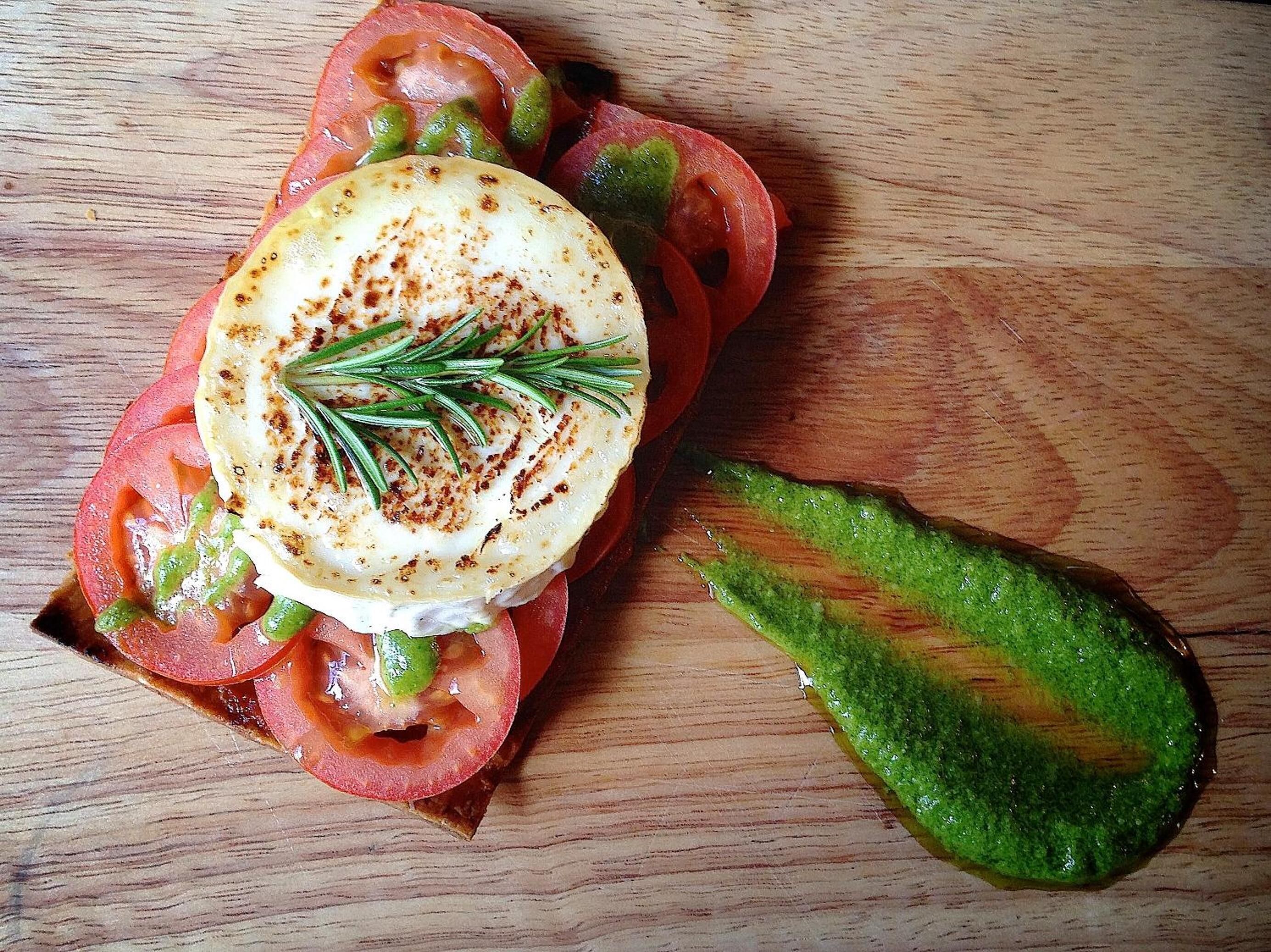 Prato com tomates fatiados, pimentões verdes e um ovo pochê por cima, decorado com alecrim, sobre uma superfície de madeira.