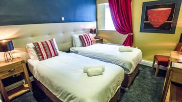 Quarto de hotel com duas camas, uma mesa de cabeceira com abajur, cortina vermelha e um quadro na parede.