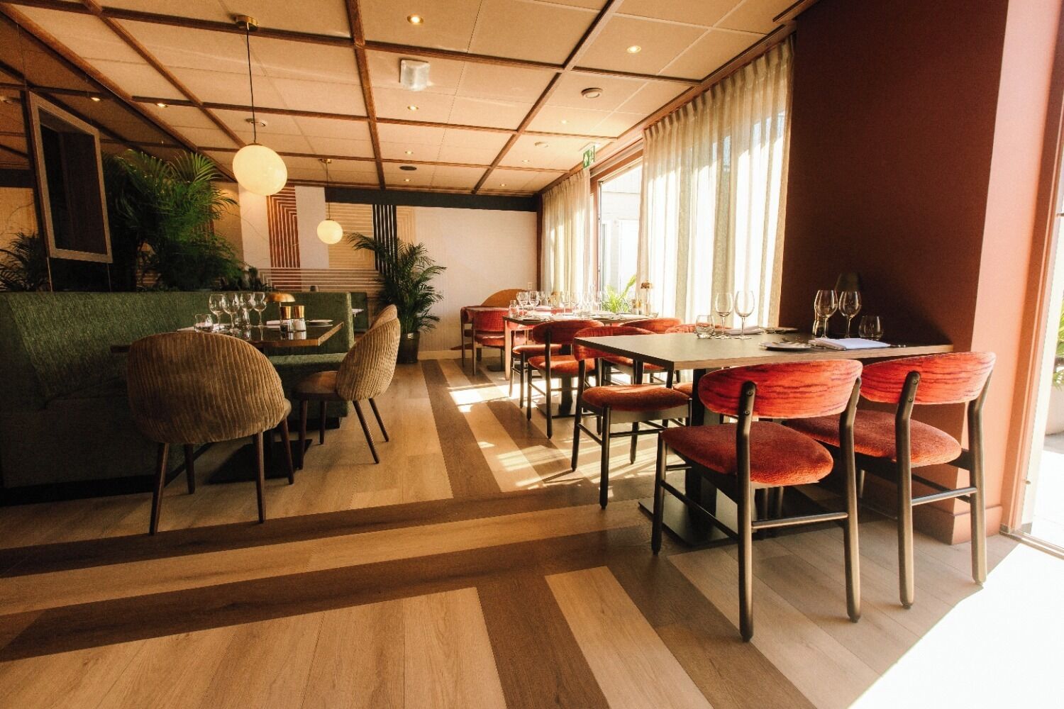 Uma sala de jantar com piso de madeira, um sofá verde e cadeiras estofadas vermelhas.