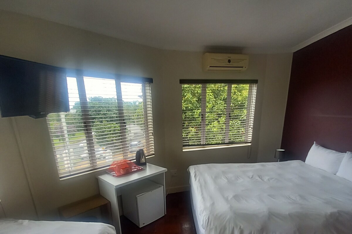 Quarto de hotel com duas camas, uma escrivaninha pequena e uma janela com persianas.