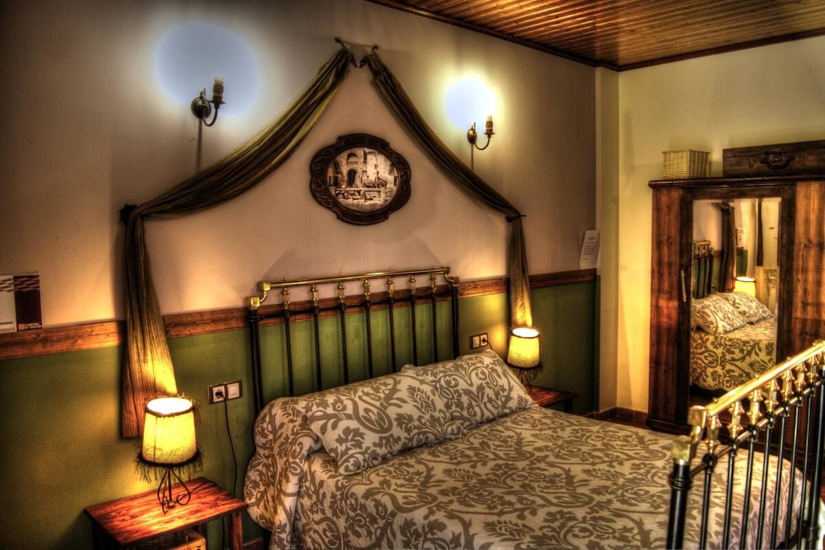 Quarto com cama, duas arandelas, um espelho e teto decorado.