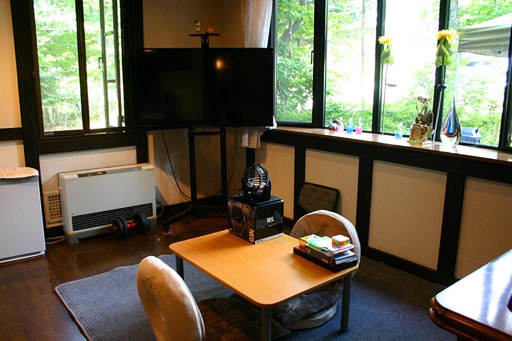 Quarto com televisão em suporte, mesa com livros, cadeira e radiador.