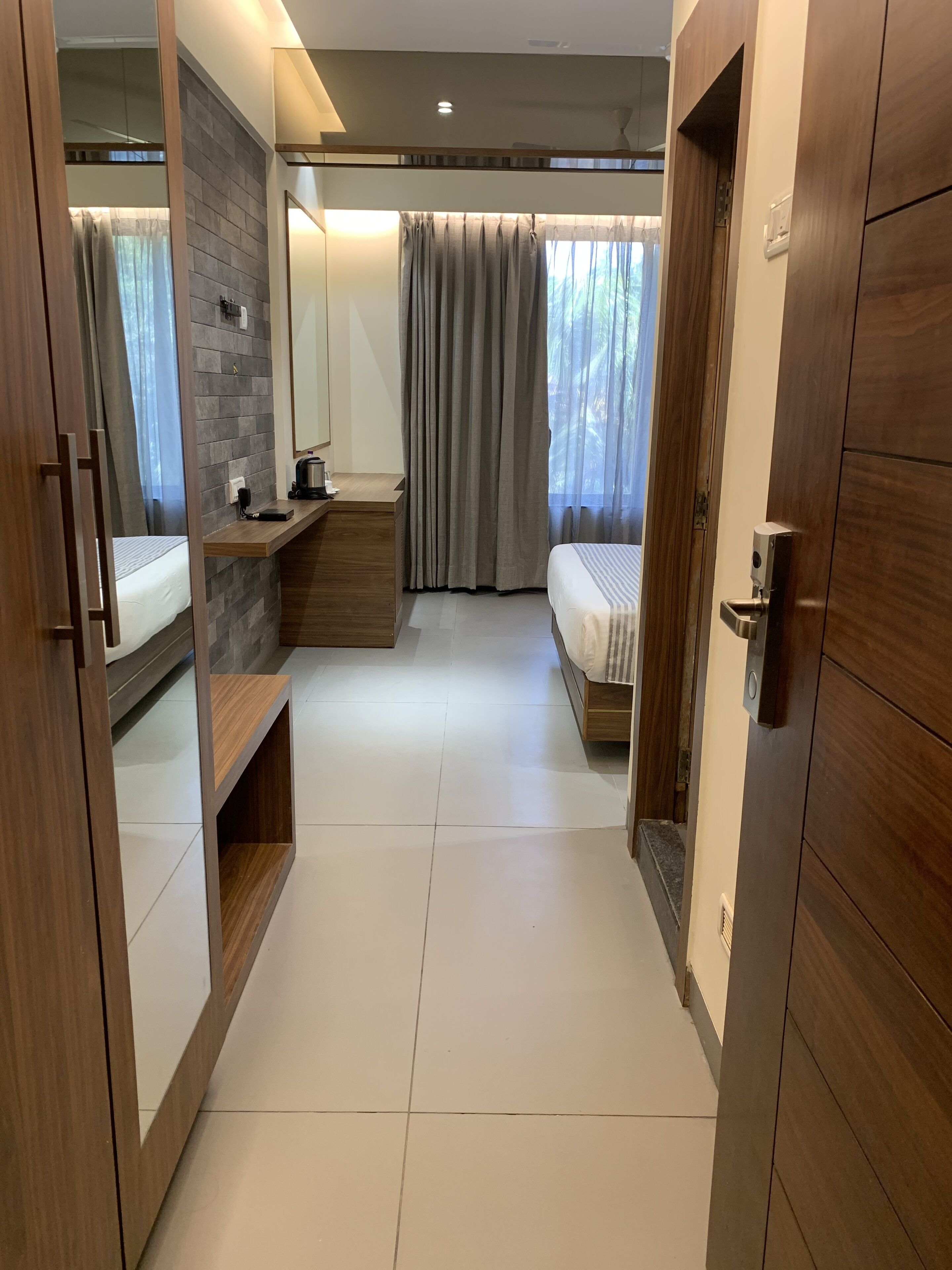 Quarto de hotel moderno com armário de madeira, secretária embutida, cama e banheiro com chuveiro e vaso sanitário.
