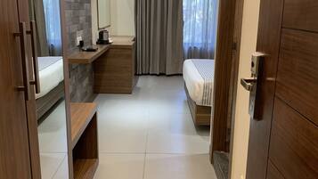 Quarto de hotel moderno com armário de madeira, secretária embutida, cama e banheiro com chuveiro e vaso sanitário.