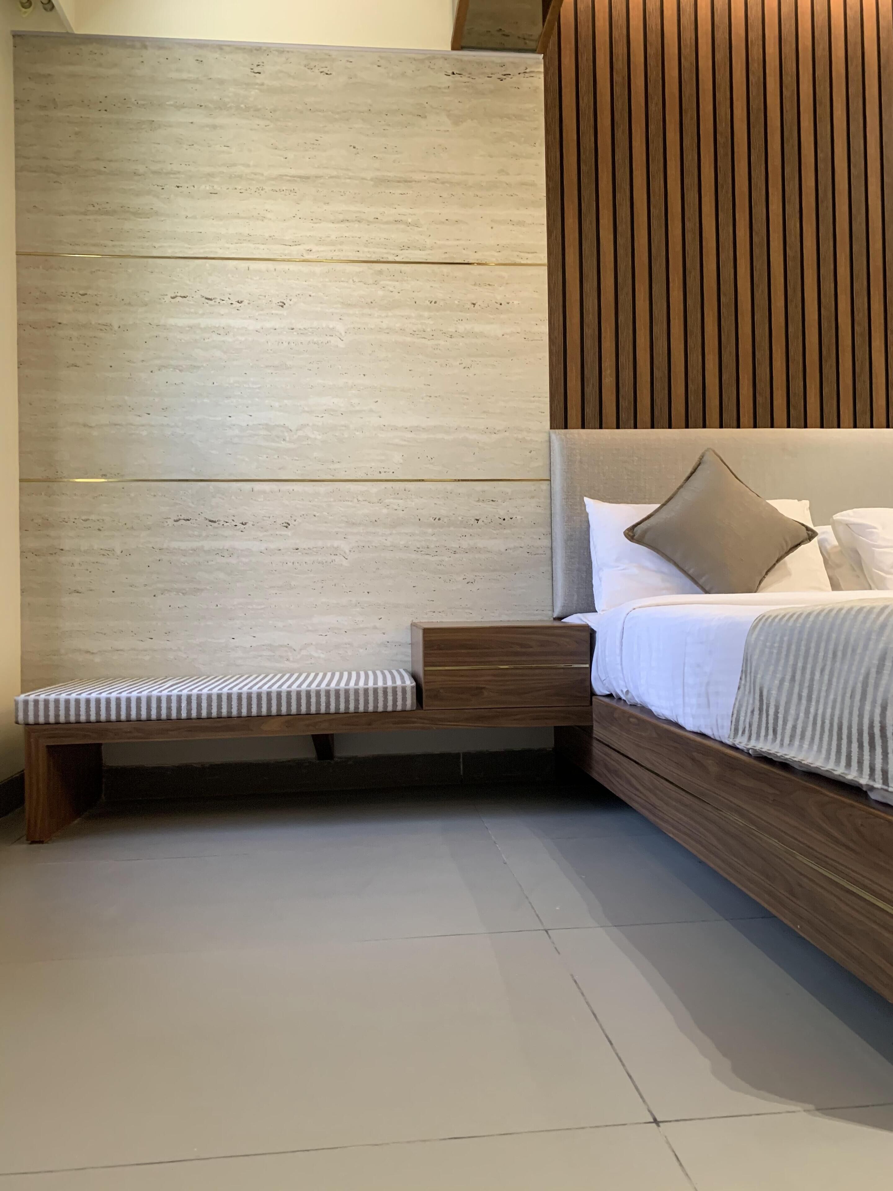 Um quarto moderno com cabeceira de madeira, um banquinho e cama com roupa de cama branca.