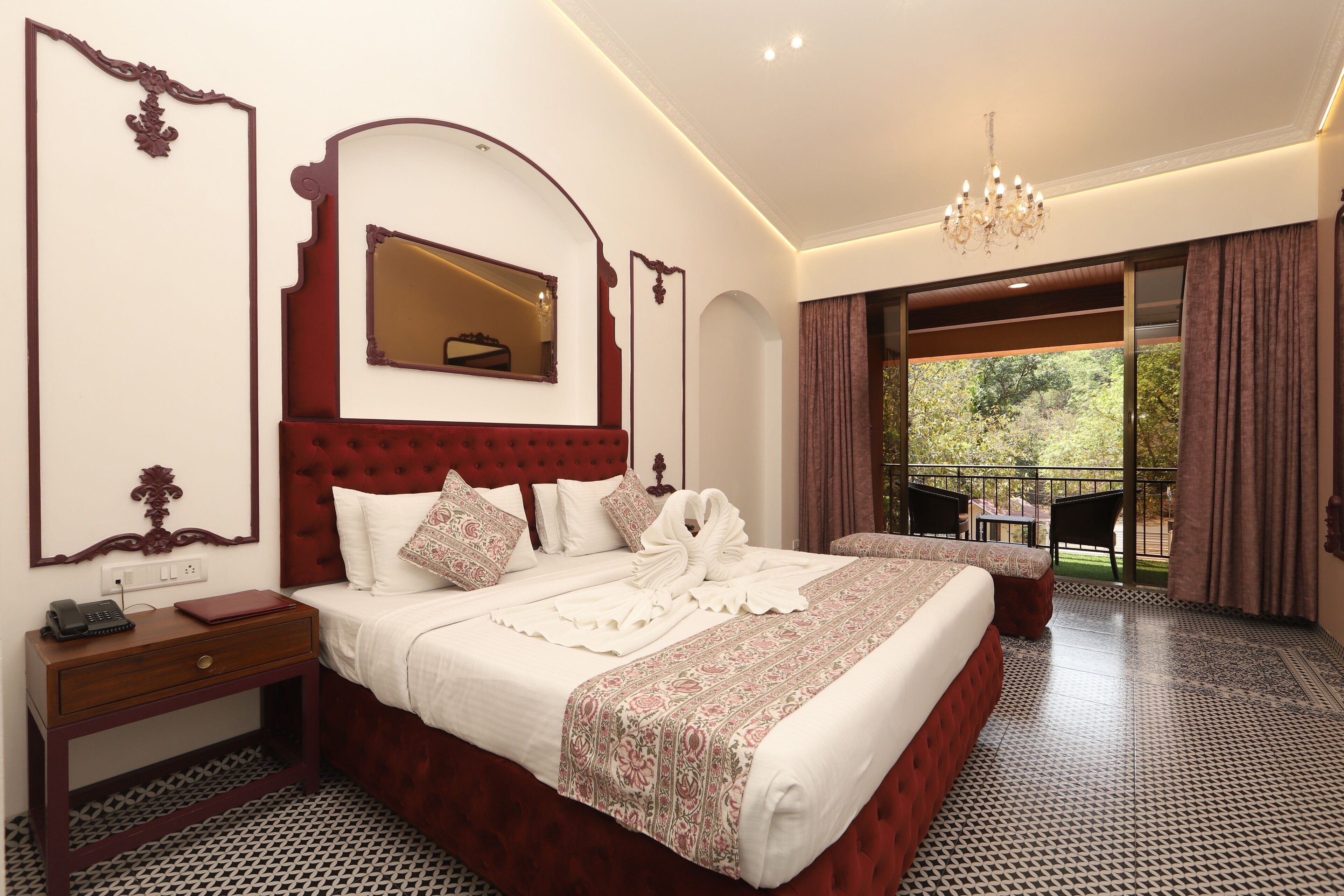 Uma cama grande com cabeceira vermelha, uma mesa de cabeceira, um espelho e vista para o exterior.