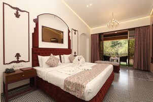 Uma cama grande com cabeceira vermelha, uma mesa de cabeceira, um espelho e vista para o exterior.