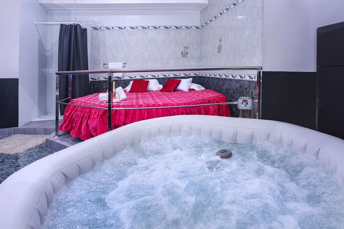 Um quarto de spa com hidromassagem, uma cama com roupa de cama vermelha e zona de duche.