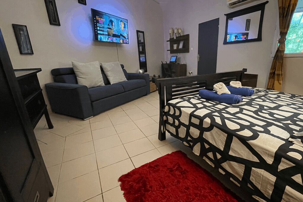 Um quarto moderno com cama, sofá, televisão e tapete vermelho.