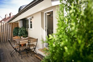 Um pátio externo com mesa e cadeiras de madeira, um vaso de planta e vista para a fachada da casa.